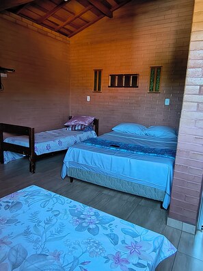 Quarto com duas camas, teto de madeira, paredes de tijolo e uma pequena janela.