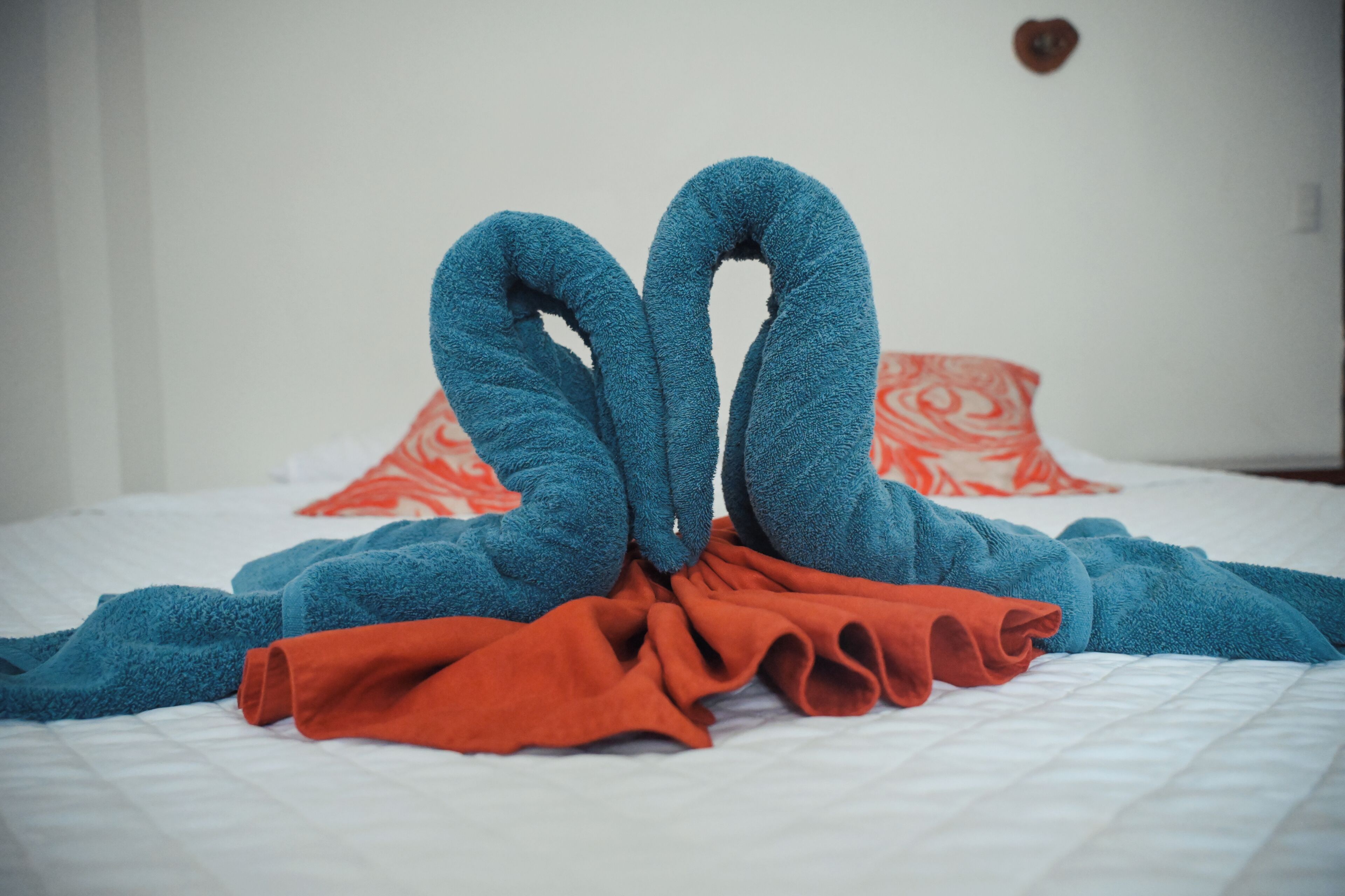 Uma cama com um edredom branco e uma almofada vermelha.