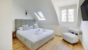 Quarto com cama, mesa de cabeceira, cadeira, janela e claraboia.