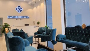 Uma área de recepção moderna com um candelabro, poltronas de veludo azul, um balcão de recepção e uma grande janela com vista.