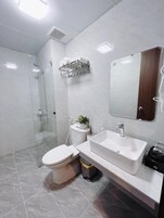Uma casa de banho moderna com cabine de duche em vidro, sanita branca, lavatório com espelho e toalheiro.
