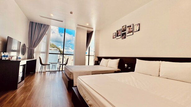 Quarto de hotel com duas camas, uma escrivaninha com televisão e uma varanda com vista para a cidade.