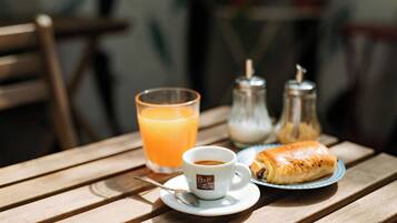 Uma mesa de madeira com uma xícara de café, um copo de suco de laranja e um pastelaria num prato.