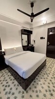 Quarto de hotel com cama, ventoinha no teto, espelho, telefone e porta.