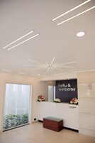Uma área de recepção de hotel com design moderno, com balcão de atendimento, um letreiro com a mensagem 'hello & welcome' e um lustre decorativo no teto.