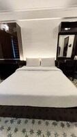 Quarto de hotel com uma cama grande, mesa de cabeceira, espelho e cômoda.