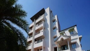 Um edifício de vários andares com telhado plano, varandas e área de entrada coberta.