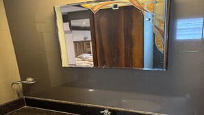Uma casa de banho com bancada de granito, uma pia branca e um espelho com moldura decorativa.