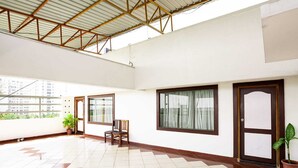 Amplo espaço interno com piso de azulejos, teto alto com vigas de metal e grandes janelas com cortinas.