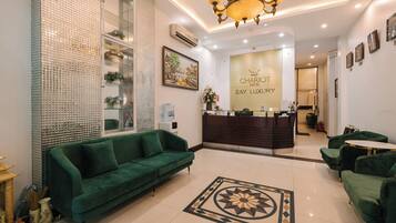 Um saguão de hotel com uma mesa de recepção, um sofá verde, um tapete estampado e um candelabro.