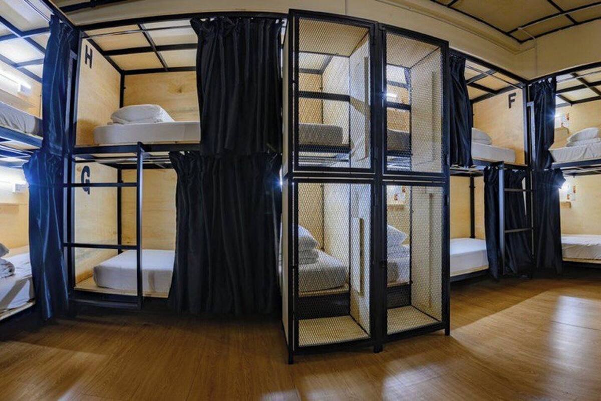 Quarto com beliches dispostos em formato circular, cada um com cortina e uma mesinha.