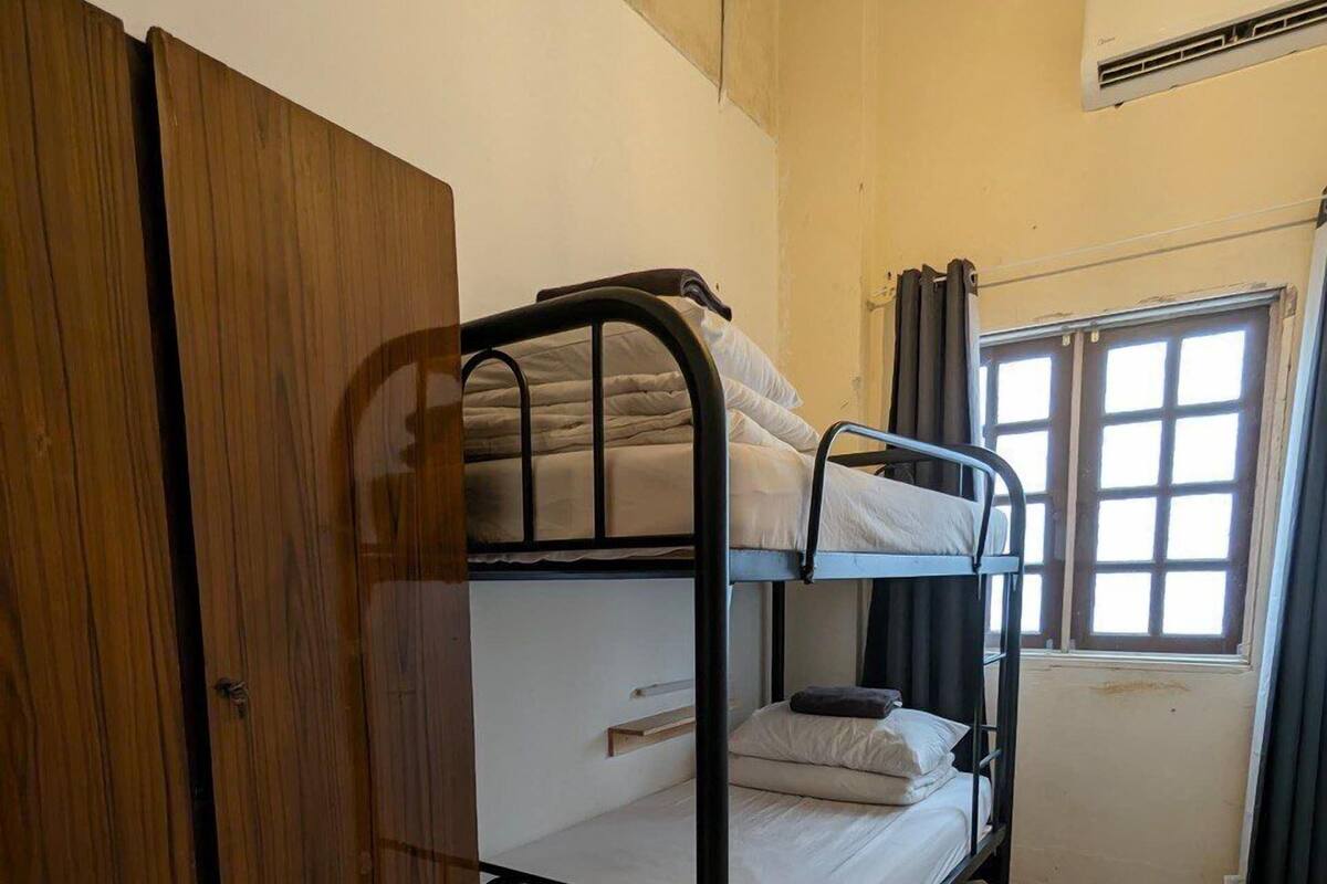 Quarto com beliche, guarda-roupa de madeira, janela com cortinas e ar condicionado.