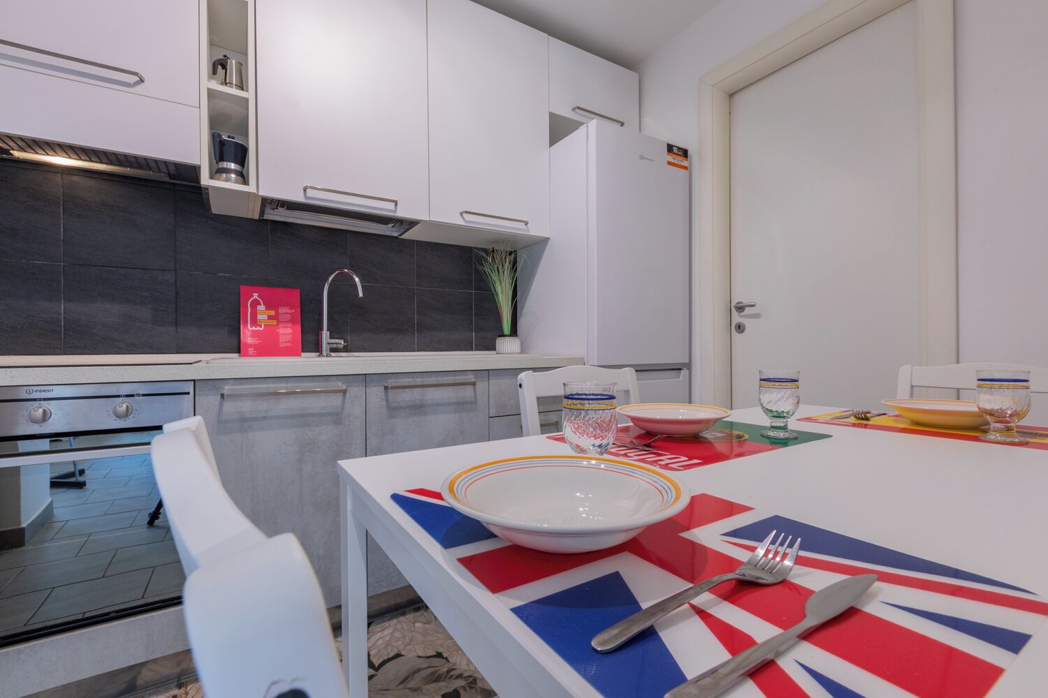 Cozinha moderna com armários brancos, fogão de aço inoxidável e área de jantar com mesa posta para dois.