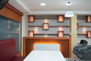 Interior moderno com mesa branca, assentos vermelhos e estantes de madeira com objetos emoldurados.