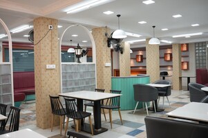 Um café moderno com mesas, cadeiras, iluminação decorativa e um design de parede estampado.