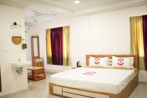 Quarto de hotel com uma cama grande, cabeceira de madeira, mesa de cabeceira, espelho, pia e uma janela com cortinas.