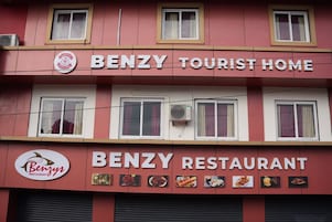 Um edifício de vários andares com a sinalização "BENZY TOURIST HOME" e "BENZY RESTAURANT", indicando um estabelecimento de hotel e restaurante.