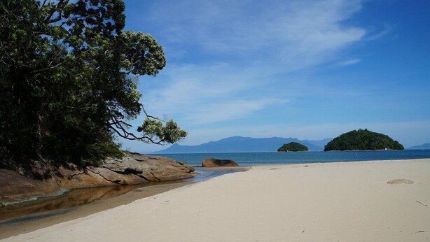 Uma praia com céu limpo, águas calmas e ilhas ao longe.