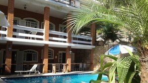 Um edifício de dois andares com piscina, móveis de exterior e palmeiras.