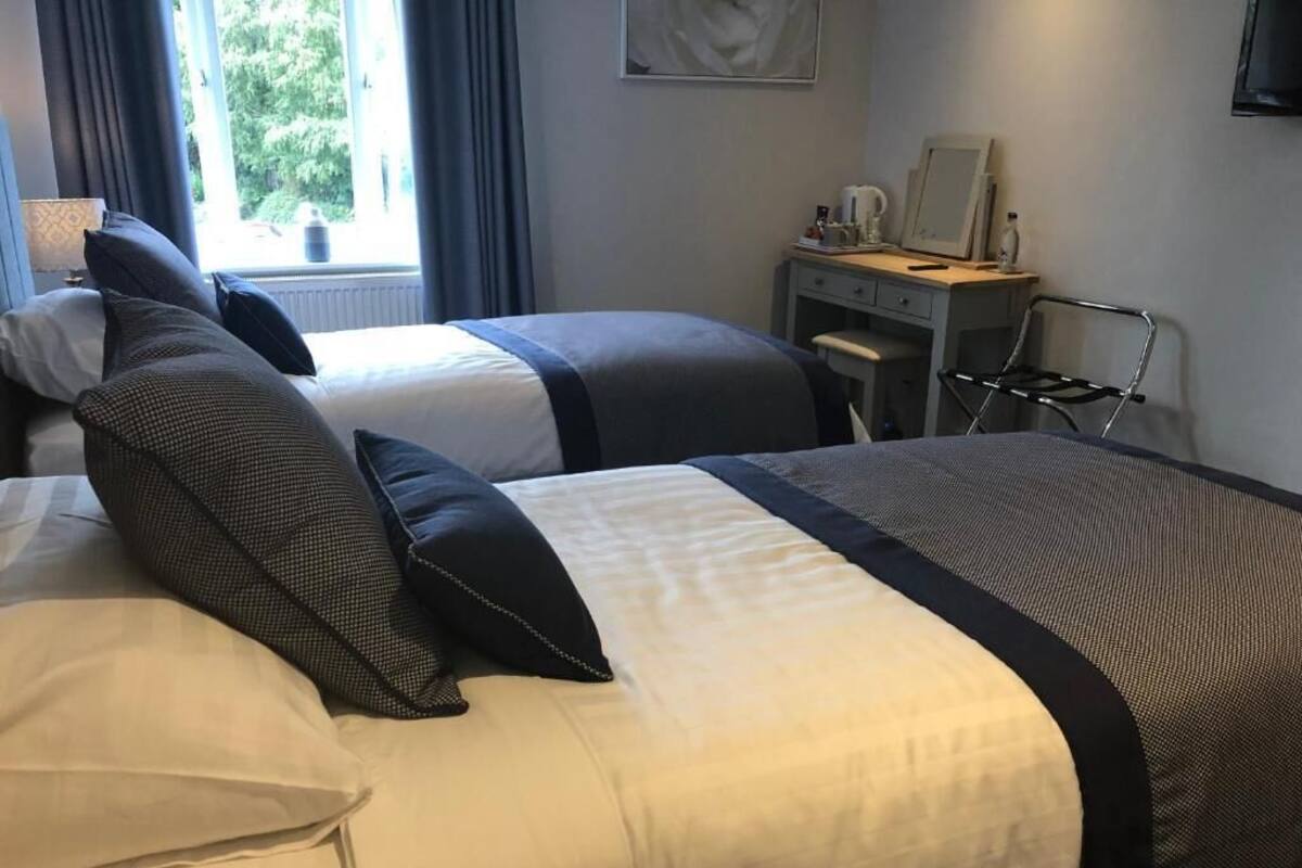 Quarto de hotel com duas camas, uma escrivaninha, uma cadeira e uma janela com cortinas.