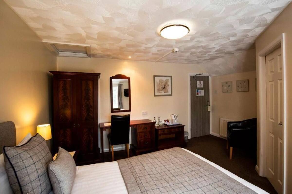 Quarto de hotel com cama, escrivaninha, guarda-roupa, espelho e radiador.
