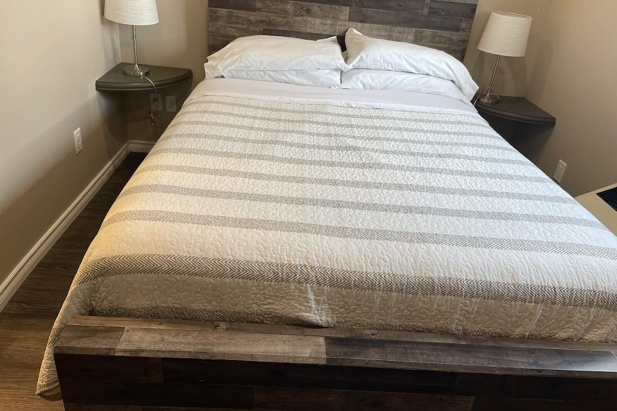 Uma cama bem arrumada com um edredom listrado, duas mesas de cabeceira com abajures e uma cabeceira de madeira.
