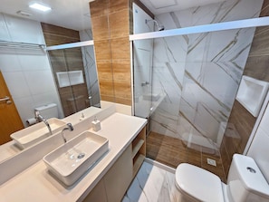 Um banheiro moderno com pia dupla, box de vidro e vaso sanitário.