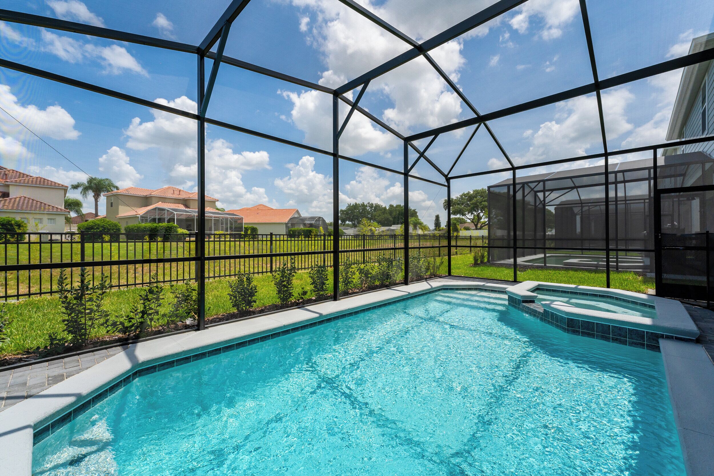 Piscina com cobertura de vidro, cercada por uma grade de metal e um gramado.