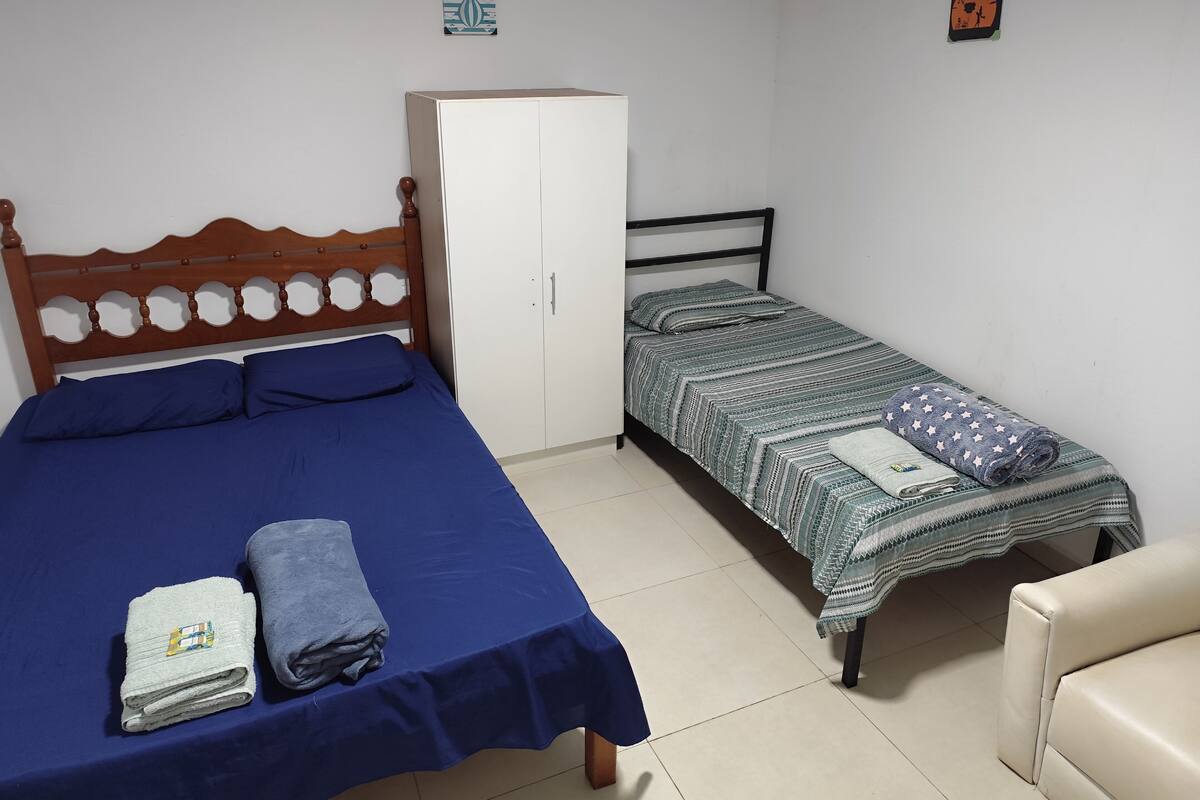Quarto com uma cama grande, uma cama menor, um guarda-roupa e uma cadeira.