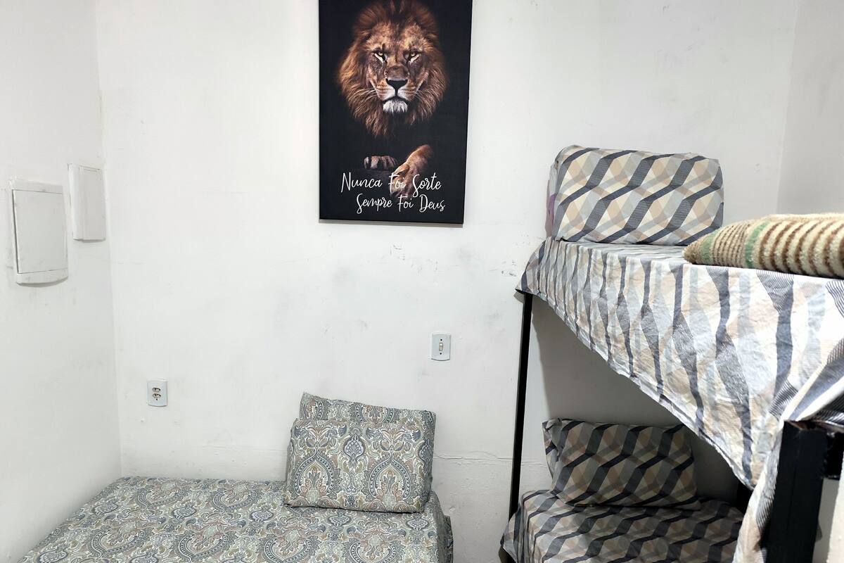 Uma cama de beliche com roupa de cama estampada, um cartaz na parede e uma tomada.