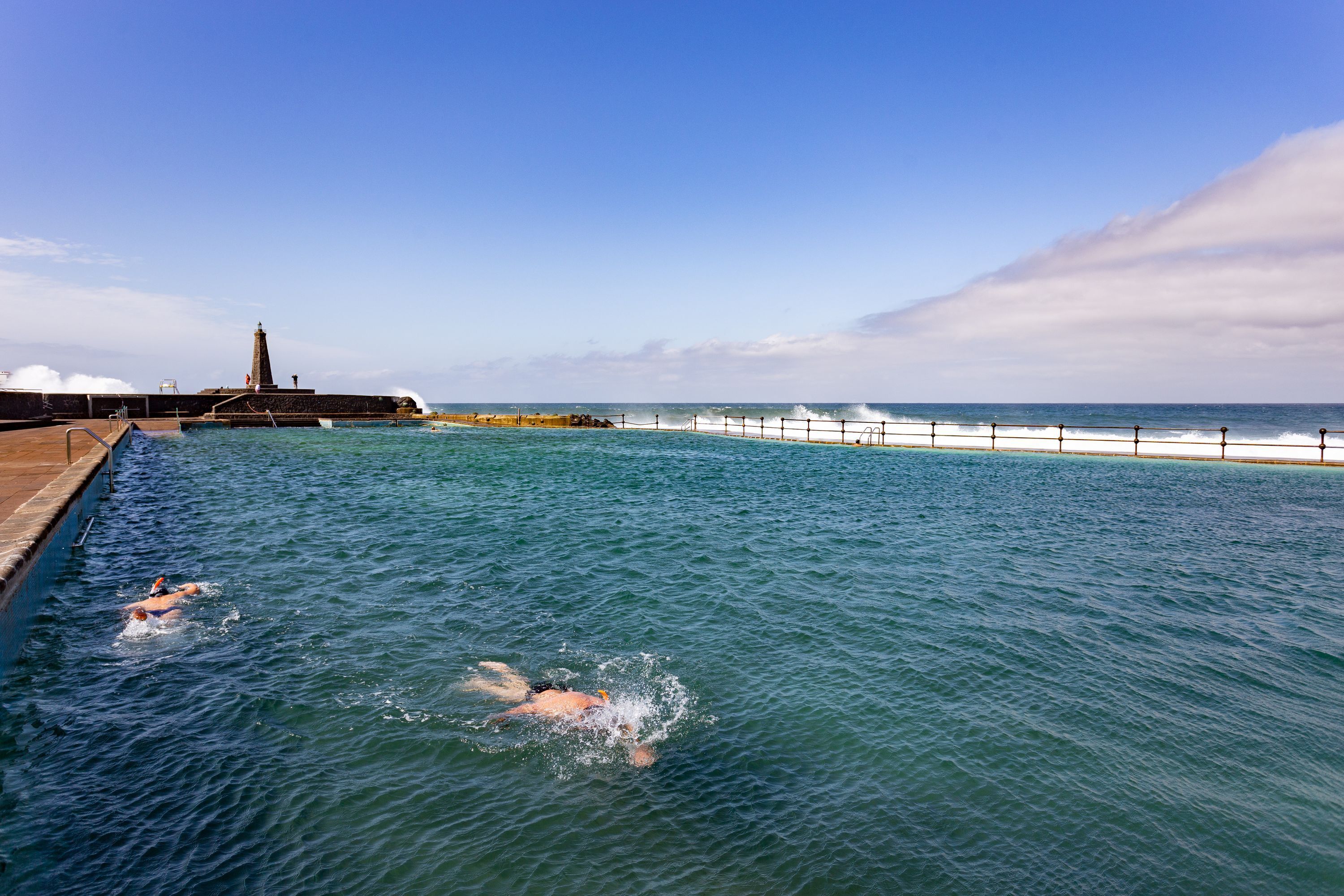 Piscina com vista para o oceano e um farol ao fundo.