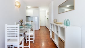 Uma cozinha moderna com armários brancos, uma área de jantar com cadeiras brancas e piso revestido de azulejos.
