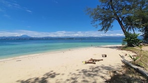 Uma praia com águas turquesa cristalinas, areal arenoso e uma grande árvore à direita.