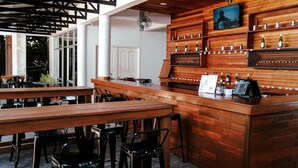 Uma área de bar com mobiliário de madeira, um balcão com garrafas e uma televisão na parede.