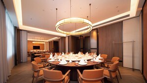 Uma sala de jantar moderna com uma mesa redonda posta para refeição, rodeada por cadeiras, e um grande candelabro circular acima.