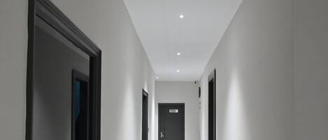 Um corredor moderno e estreito, com paredes brancas e molduras de porta escuras, que leva a uma porta identificada com a palavra 'STORE'.