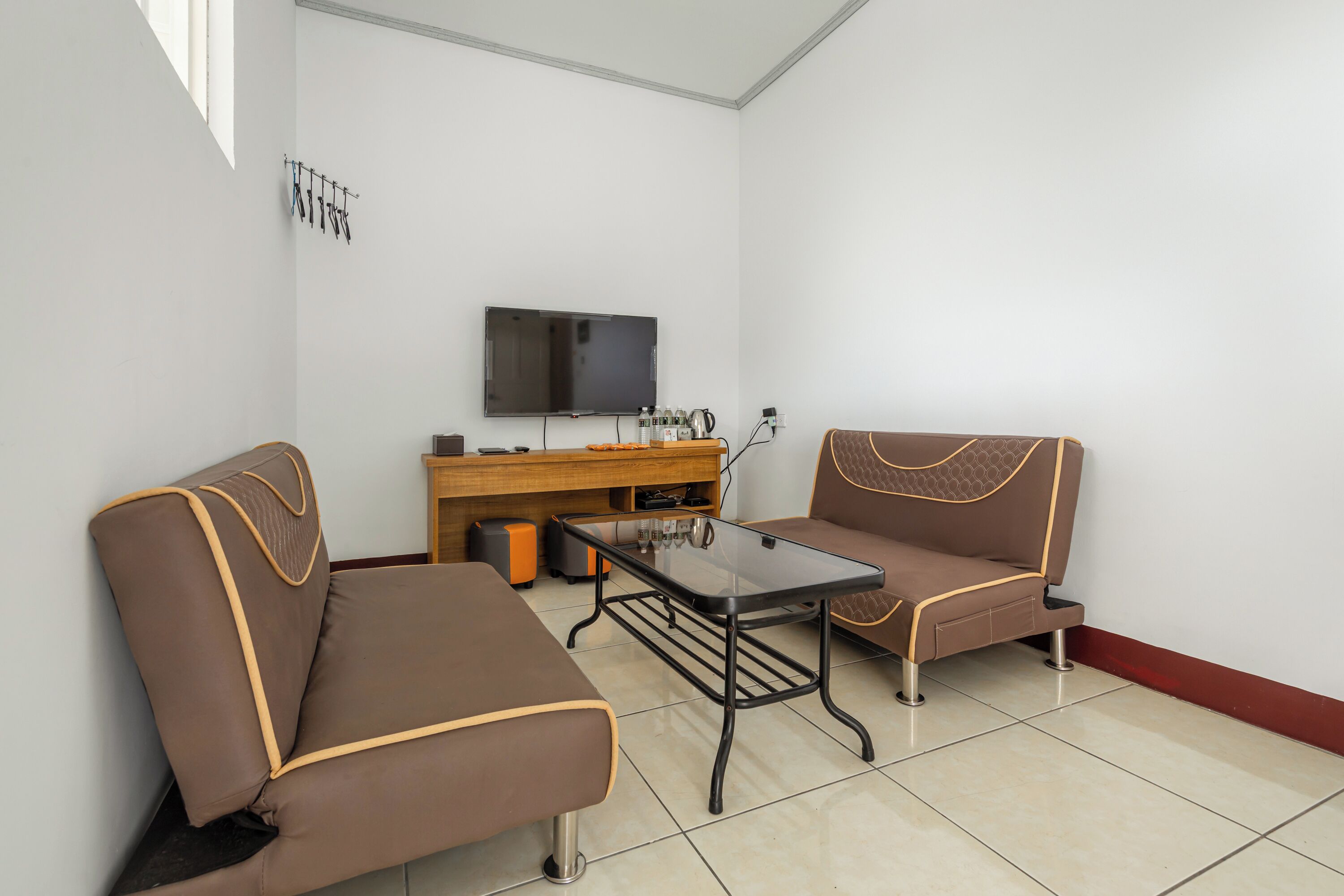 Uma sala de estar com dois sofás marrons, uma mesa de centro de vidro, uma televisão na parede e um armário de madeira.