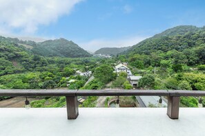 Vista de uma varanda com guarda-corpo, com vista para um vale coberto de vegetação exuberante e um edifício com telhado vermelho.
