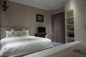 Quarto de hotel com uma cama grande, escrivaninha, cadeira, televisão e guarda-roupa.