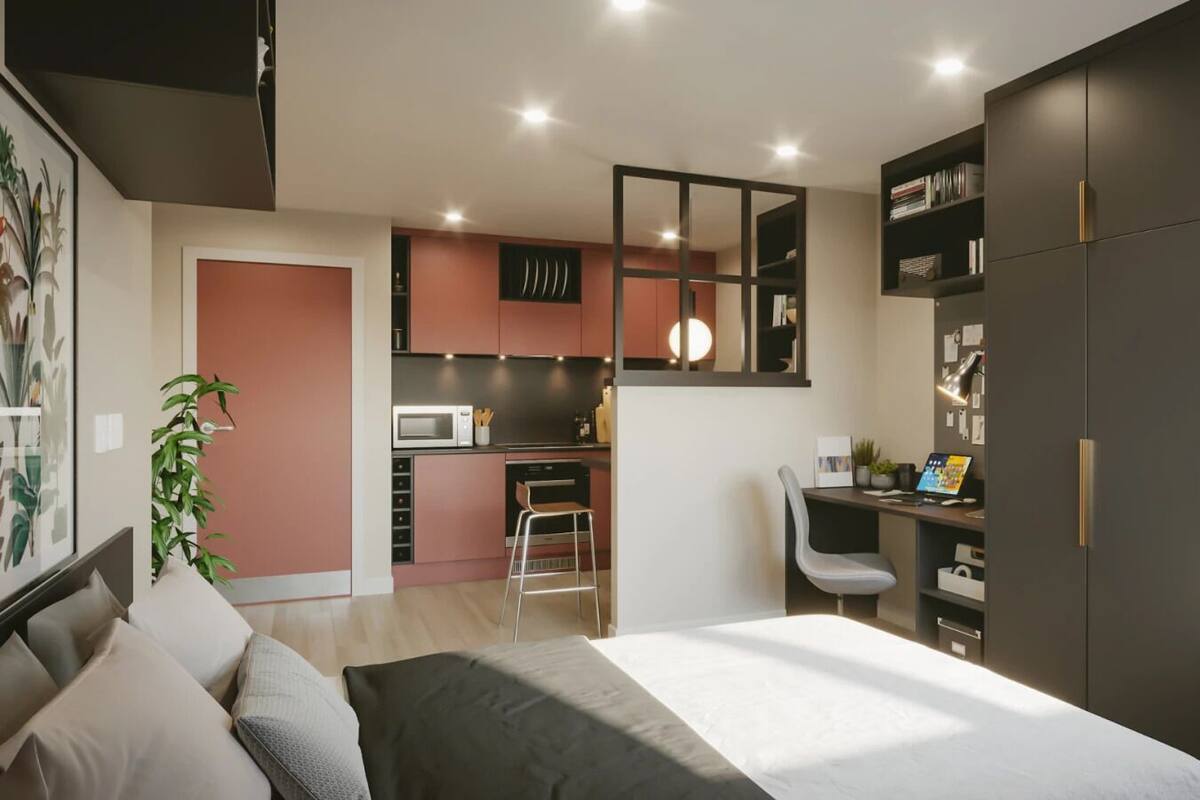 Quarto moderno com uma cama grande, uma escrivaninha e uma kitchenette ao fundo.