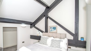 Quarto com cama, mesa de cabeceira, penteadeira, quadro na parede e porta que dá para outro cômodo.