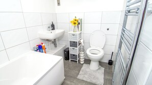 Casa de banho moderna com banheira branca, pia, sanita e área de duche.