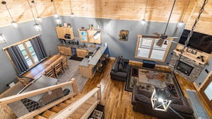 Uma sala de estar espaçosa com teto de madeira, cozinha com armários de madeira, área de refeições e lareira.