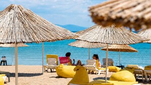 Uma praia com espreguiçadeiras e guarda-sóis de palha.