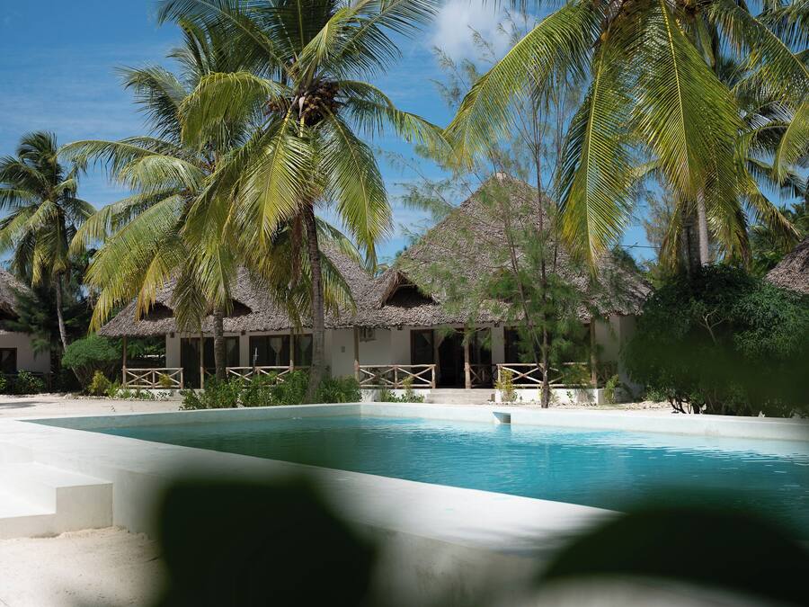 Um resort com bangalôs de telhado de palha, piscina e palmeiras.
