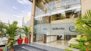 Entrada de hotel com fachada de vidro, plantas em vasos e balcão de recepção.