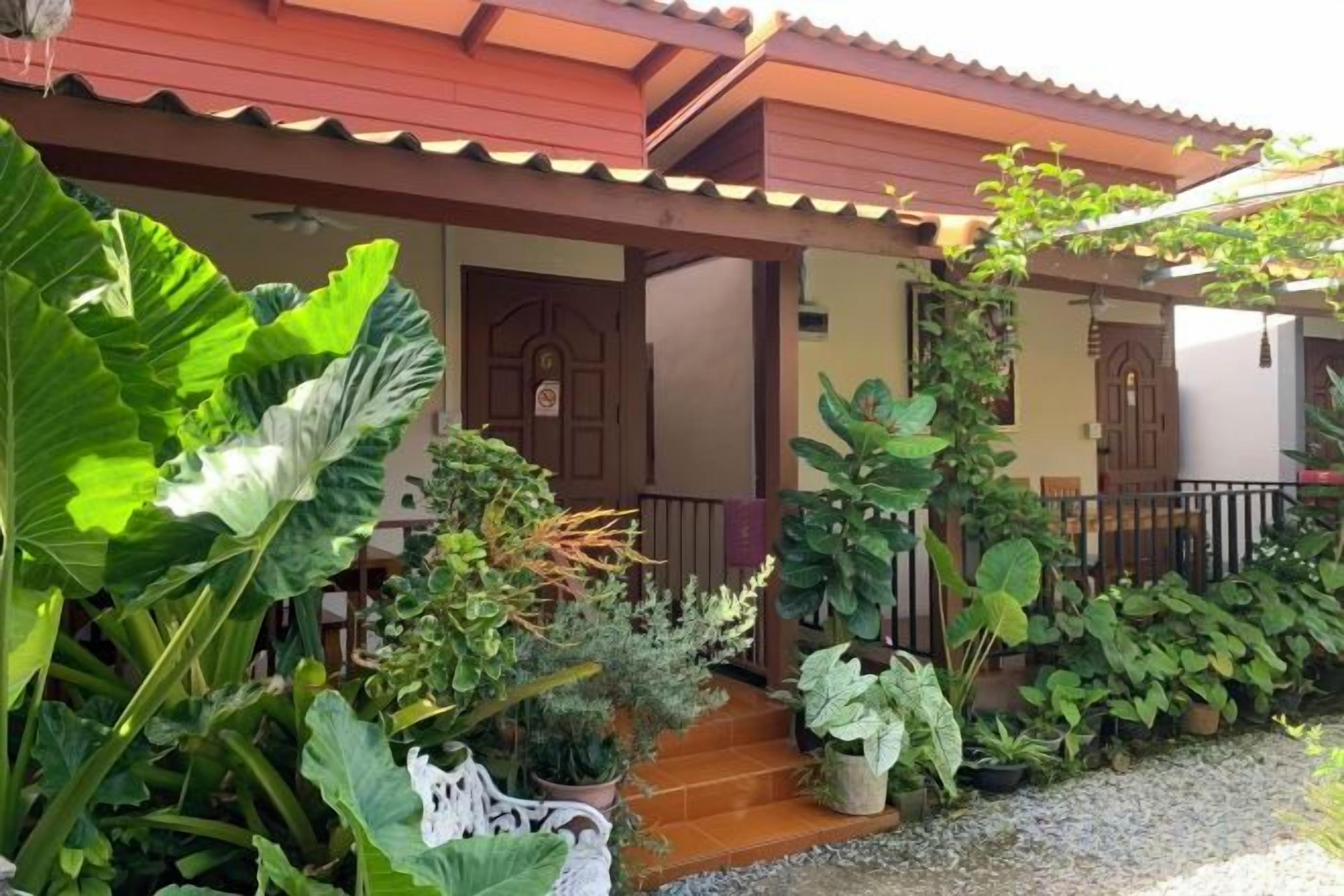 Uma casa com varanda, plantas grandes e uma porta.