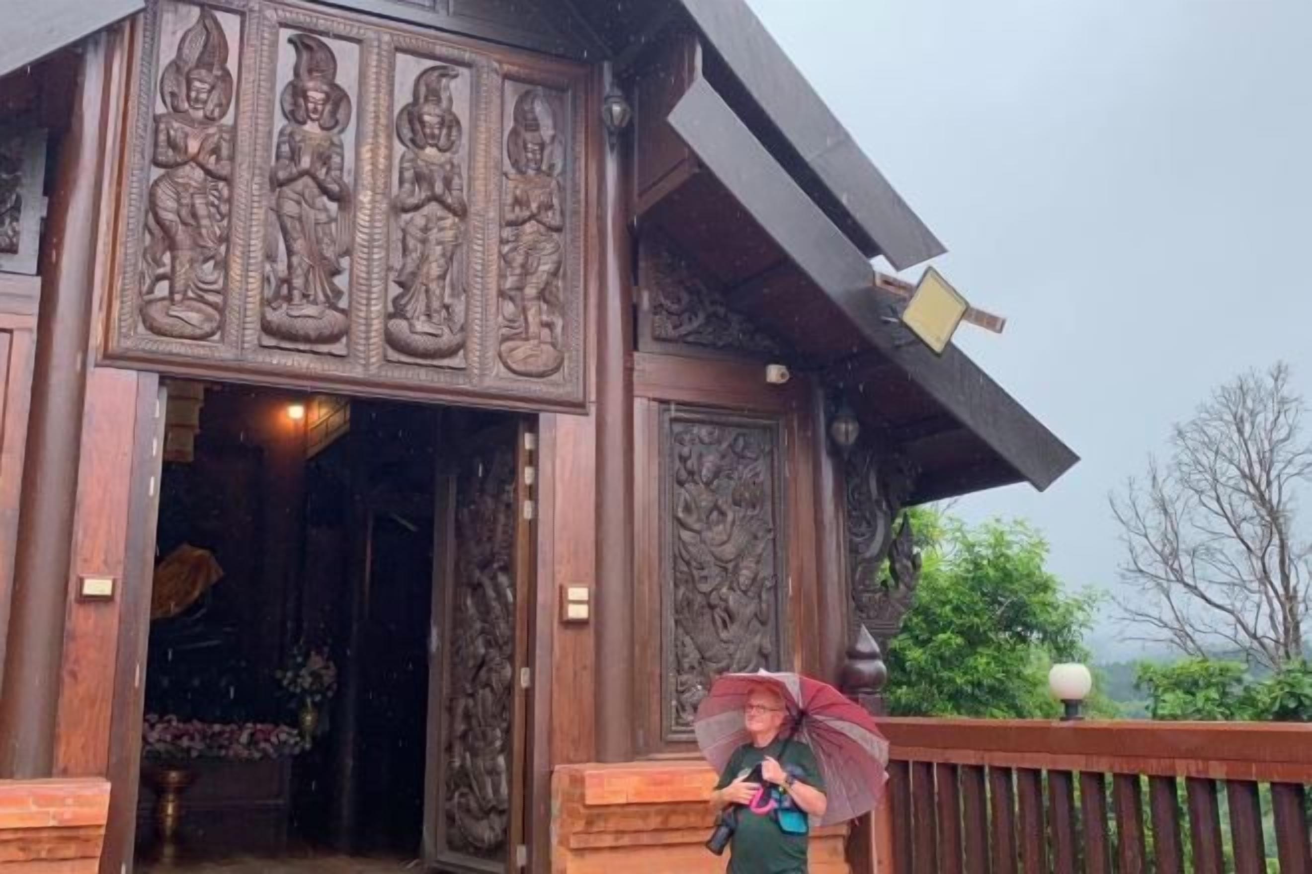 Estrutura de madeira com entalhes elaborados, uma entrada coberta e uma pessoa segurando um guarda-chuva.