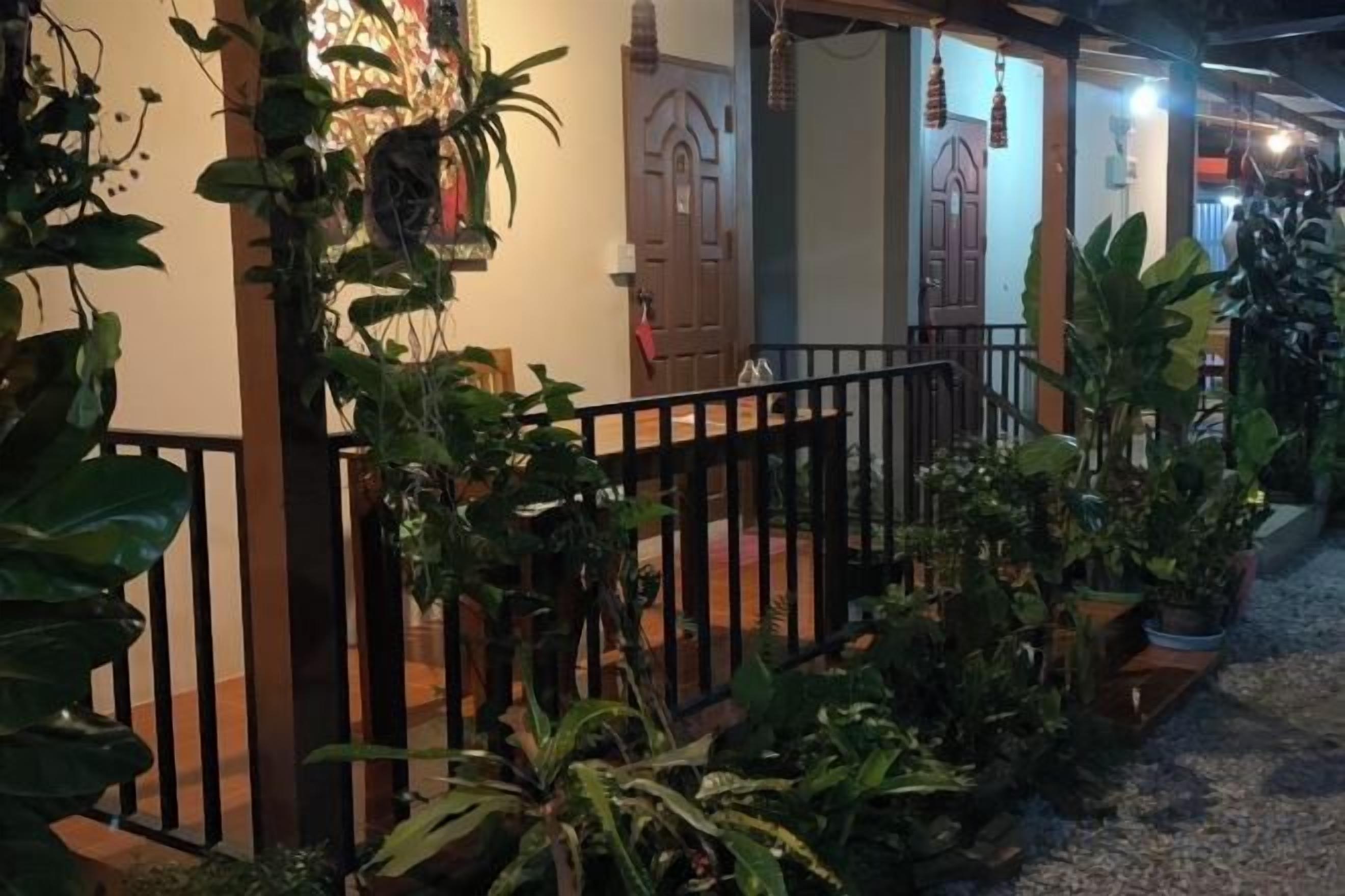 Corredor de hotel com plantas em vasos, corrimão de madeira e porta com design tradicional.
