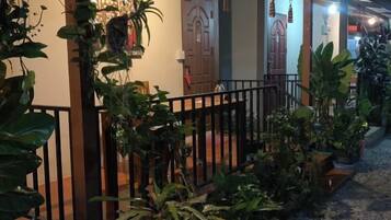 Corredor de hotel com plantas em vasos, corrimão de madeira e porta com design tradicional.